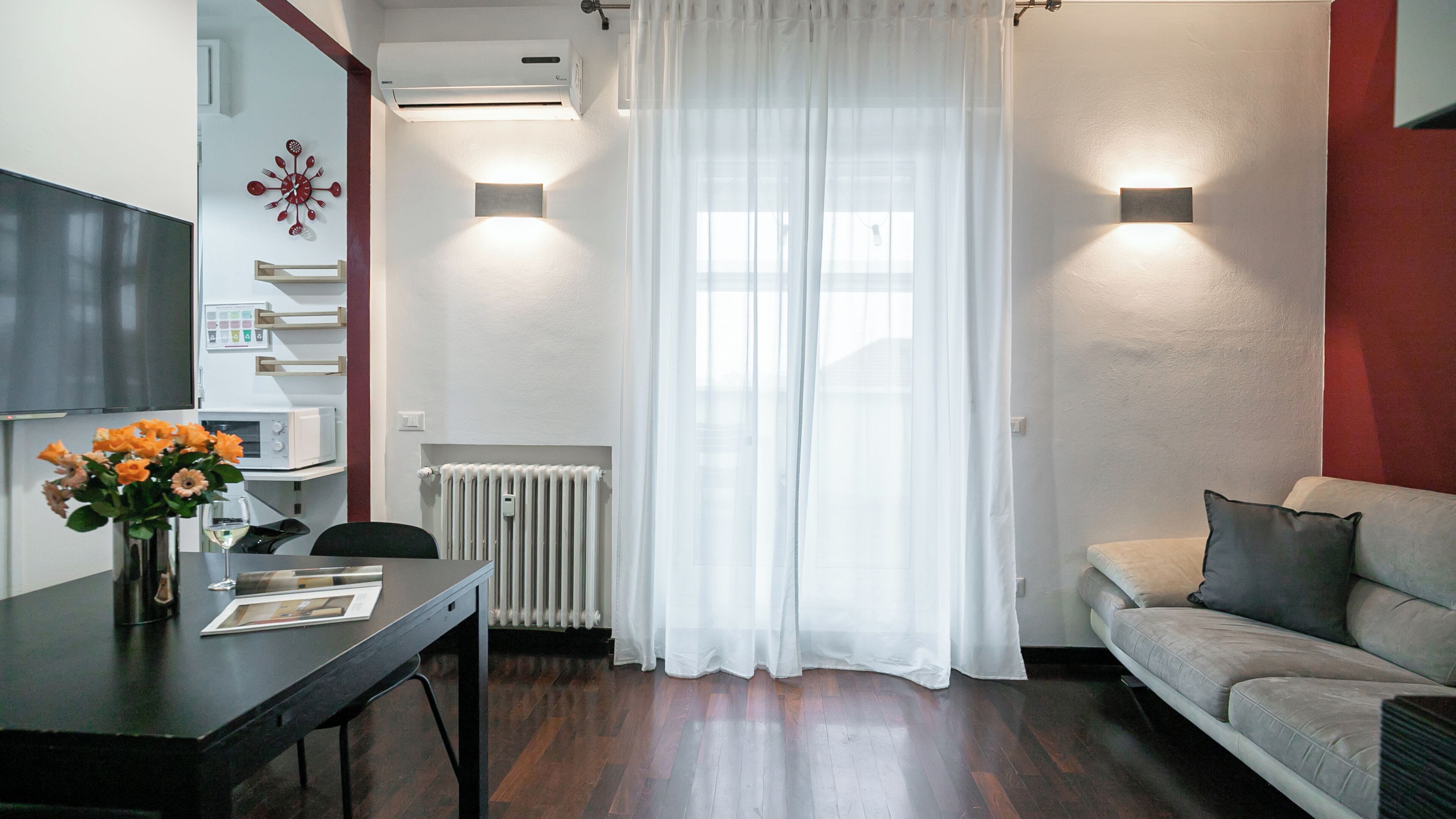 Uma sala de estar moderna com uma mesa de jantar, um sofá, um radiador e uma janela com cortinas leves.