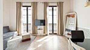 Quarto de hotel com sofá, uma mesinha, televisão e varanda com guarda-corrimão.