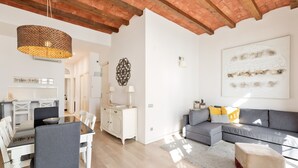 Uma sala de estar ampla com área de jantar, um sofá cinza e uma mesa de jantar branca com cadeiras.