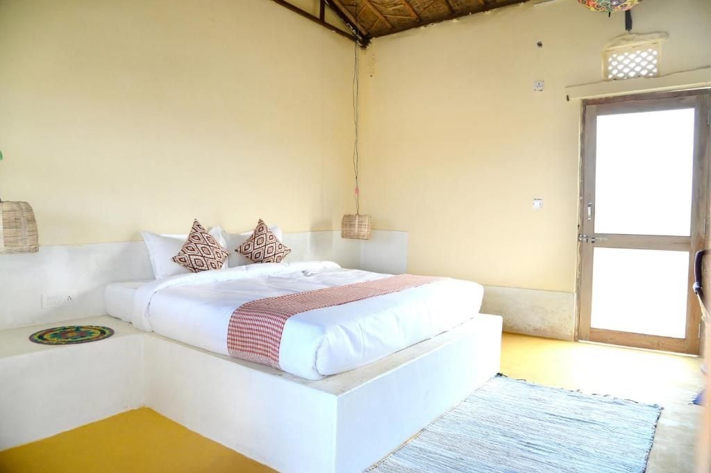 Quarto de casal com cama de solteiro, almofadas estampadas, mesa redonda pequena e porta com vista.