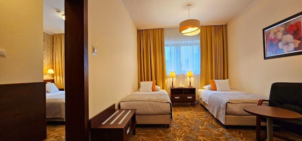 Quarto de hotel com duas camas de solteiro, um sofá, uma mesa pequena e uma cadeira.