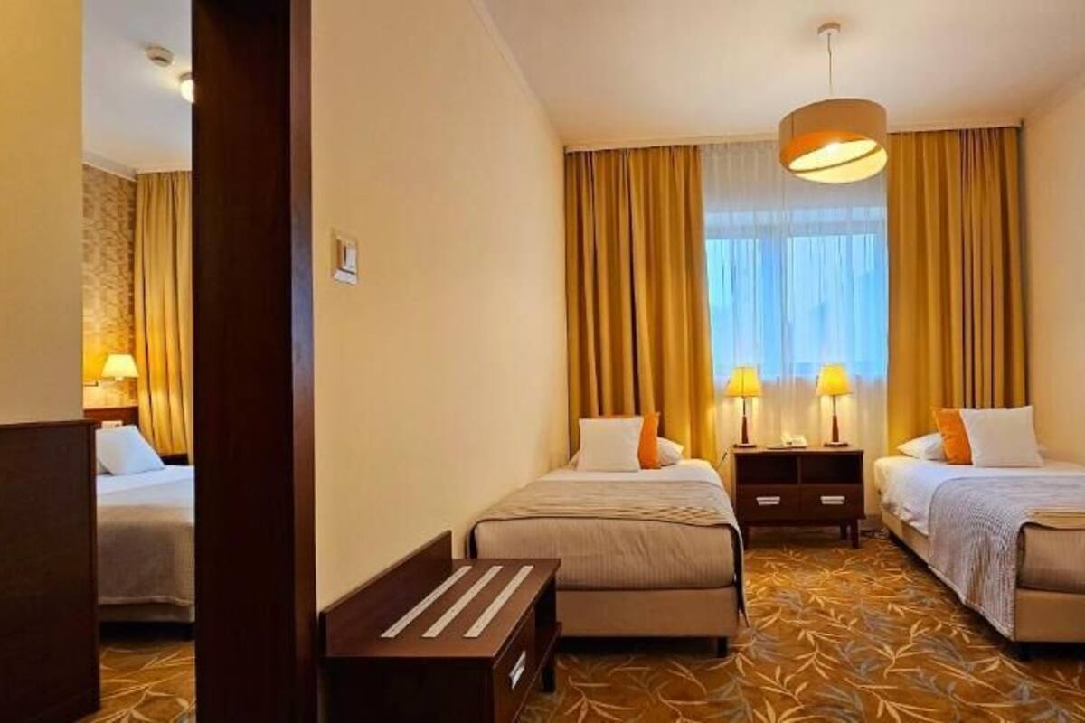 Quarto de hotel com duas camas de solteiro, um sofá, uma mesa pequena e uma cadeira.