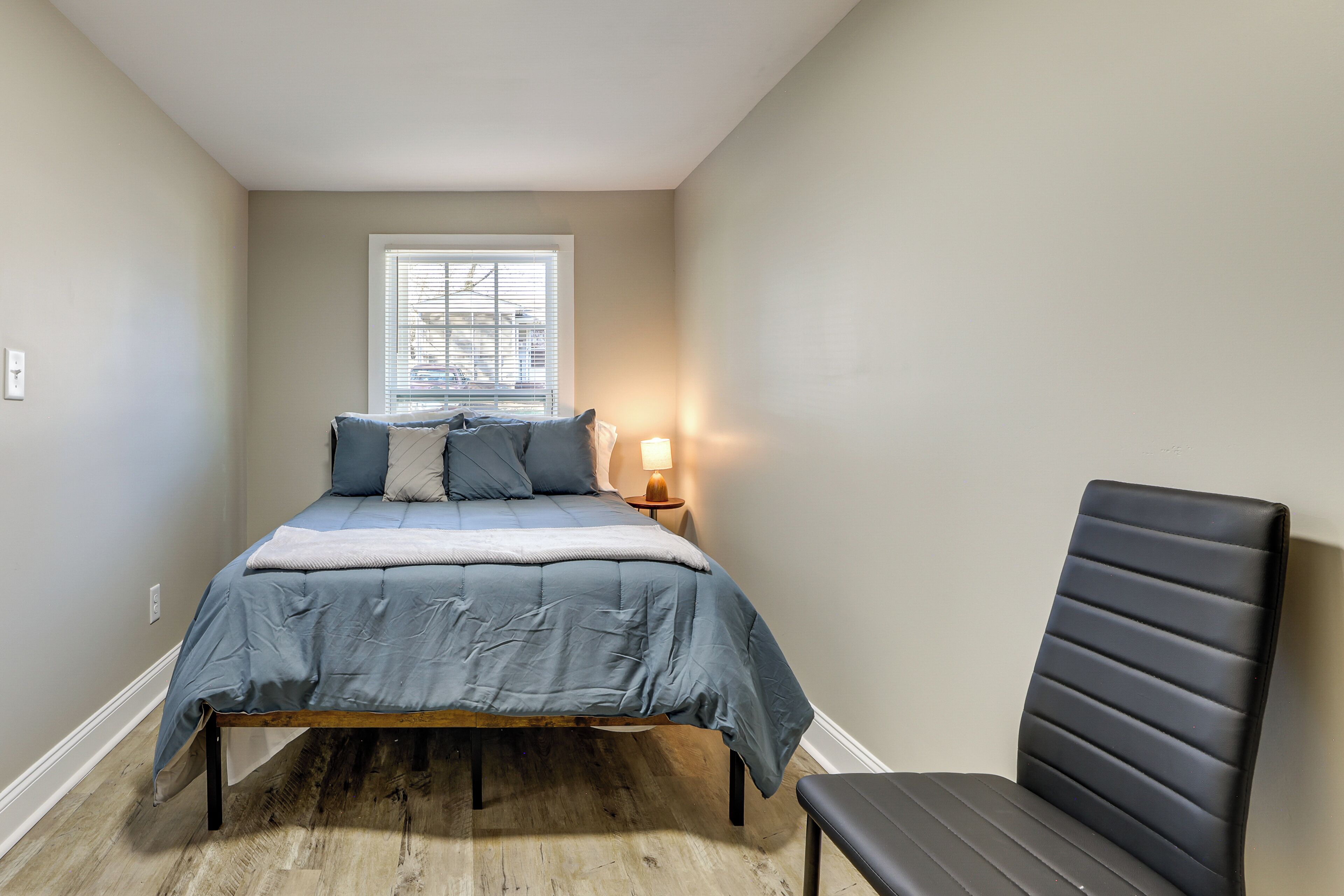 Um quarto com uma cama, mesa de cabeceira, abajur e uma cadeira.