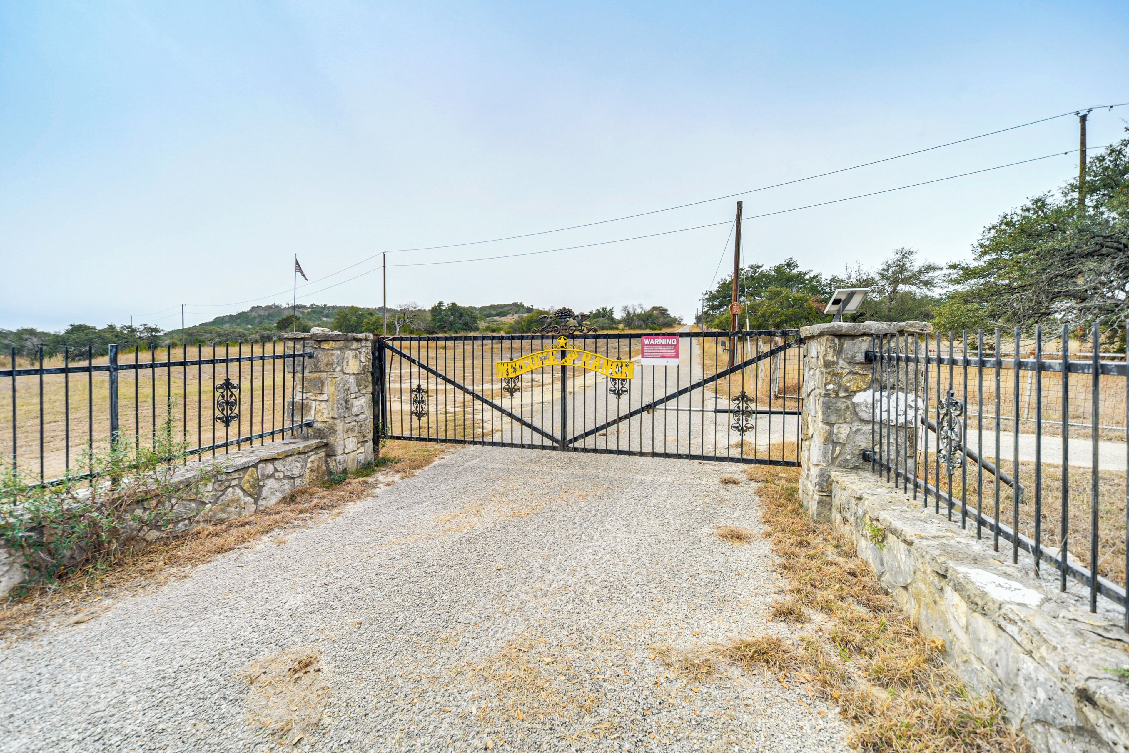 Uma entrada com portão e aviso, uma parede de pedra e um caminho de cascalho que leva a uma área cercada.