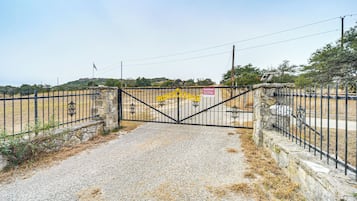 Uma entrada com portão e aviso, uma parede de pedra e um caminho de cascalho que leva a uma área cercada.