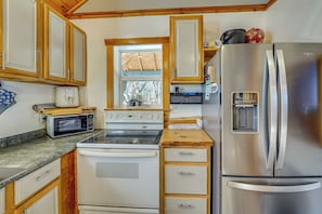 Cozinha compacta com armários de madeira, geladeira de aço inoxidável, micro-ondas, forno e janela com vista para árvores.