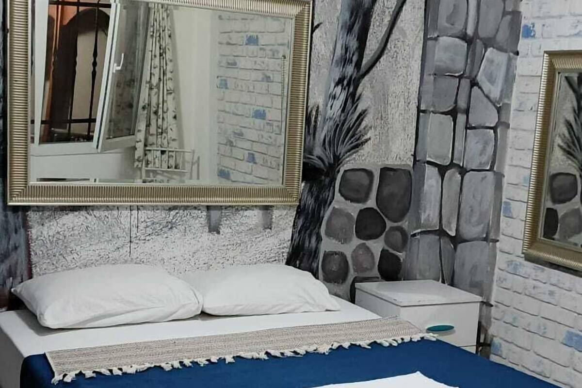 Quarto com cama, mesa de cabeceira, espelho e um mural na parede.