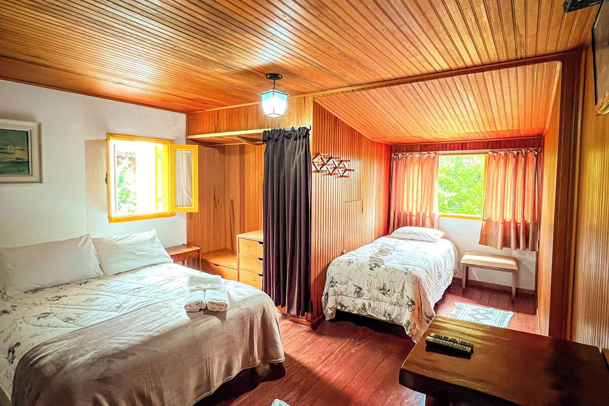 Quarto com duas camas, teto de madeira e uma pequena mesa com controle remoto.