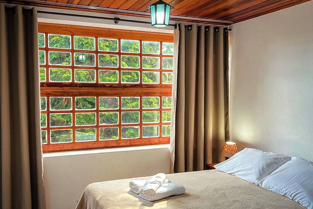 Quarto com uma janela grande, uma cama e uma mesa de cabeceira com abajur.