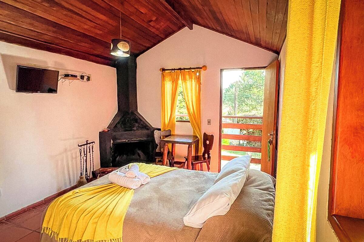 Um quarto aconchegante com uma cama, uma mesa, uma cadeira, uma lareira e uma janela com cortinas.