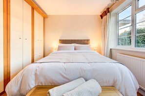 Uma cama bem arrumada com cabeceira de madeira, uma mesa de cabeceira com abajur e uma janela com cortinas.