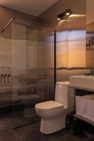 Uma casa de banho moderna com cabine de duche em vidro, sanita branca e toucador com espelho.