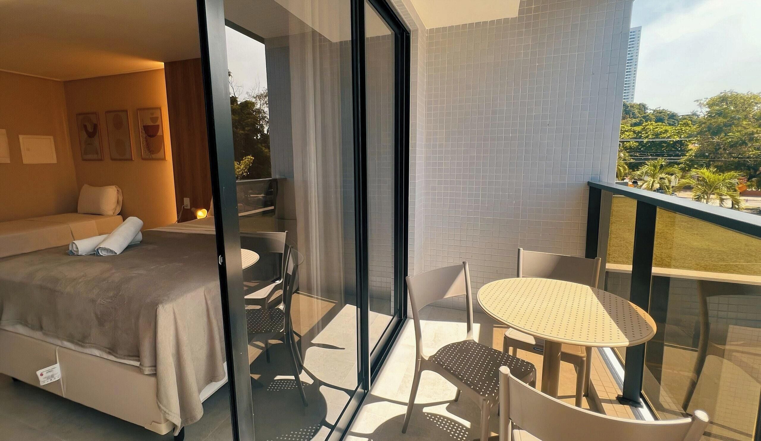 Quarto de hotel moderno com uma cama, varanda com mesa e cadeiras e vista para o exterior.
