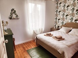 Quarto com cama, mesa de cabeceira, penteadeira e janela com cortinas leves.
