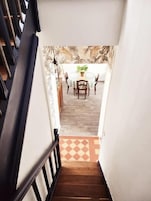 Escadaria que leva a uma área de refeições com mesa e cadeiras, um vaso de planta e um chão estampado.