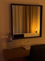 Quarto de hotel com um espelho grande, uma garrafa de água e dois copos sobre uma mesa de madeira.