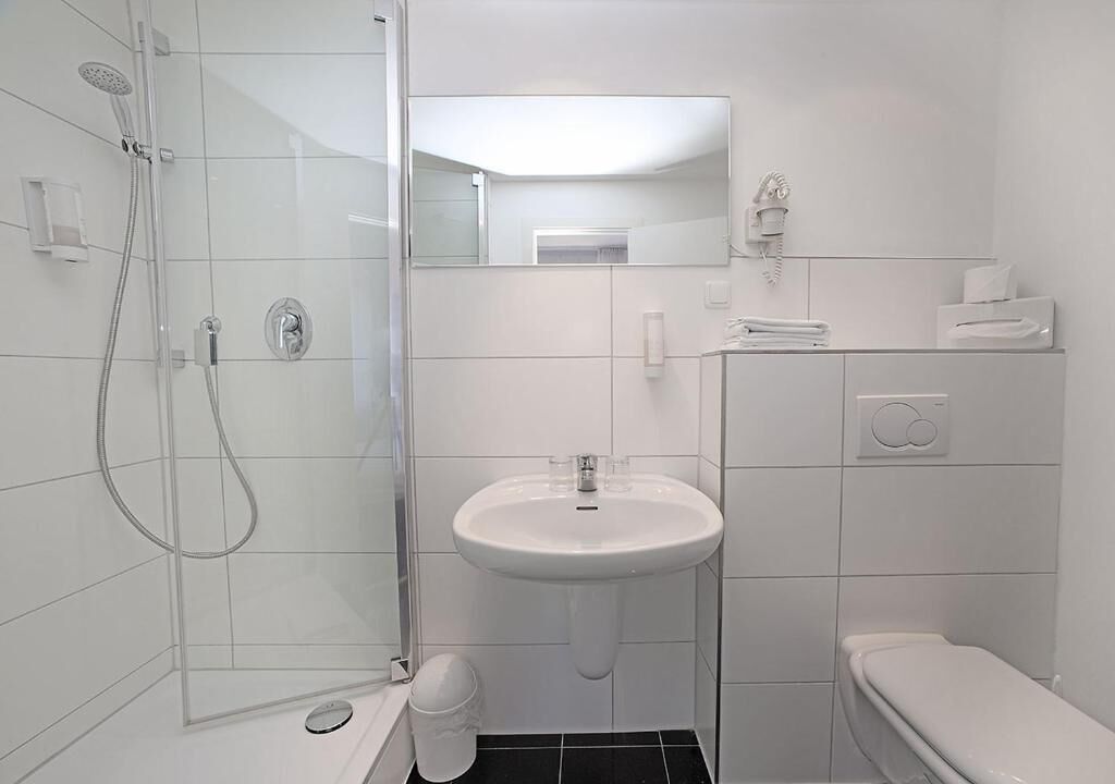 Uma casa de banho moderna com cabine de chuveiro em vidro, lavatório branco, sanita e espelho.