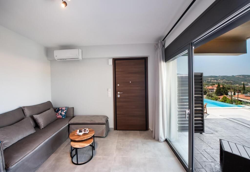 Sala de estar moderna com sofá, uma mesinha e porta que dá para uma varanda com vista para a piscina.