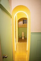 Um corredor estreito com um arco iluminado em amarelo que dá para um banheiro com vaso sanitário e janela.