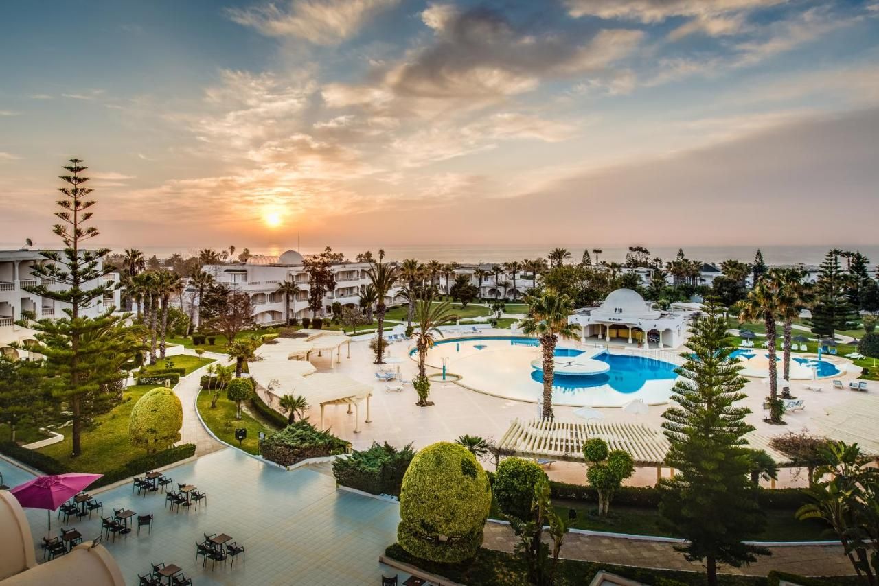 Resort com várias piscinas, um jardim bem cuidado e vista para o oceano ao pôr do sol.