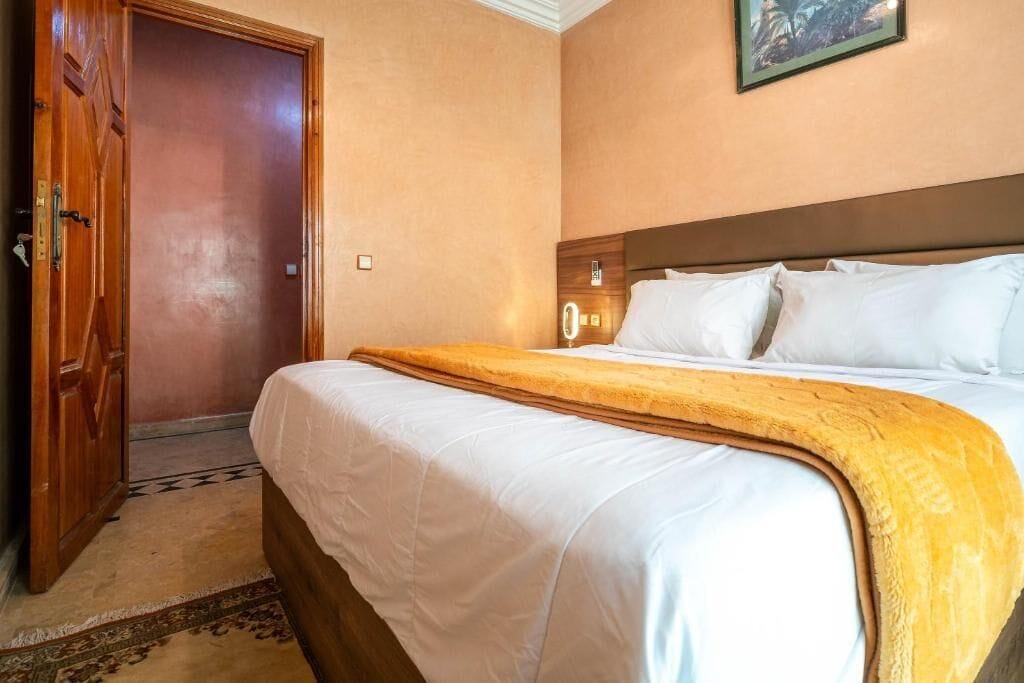 Quarto de hotel com uma cama grande, cabeceira de madeira e uma porta.