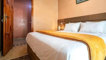 Quarto de hotel com uma cama grande, cabeceira de madeira e uma porta.