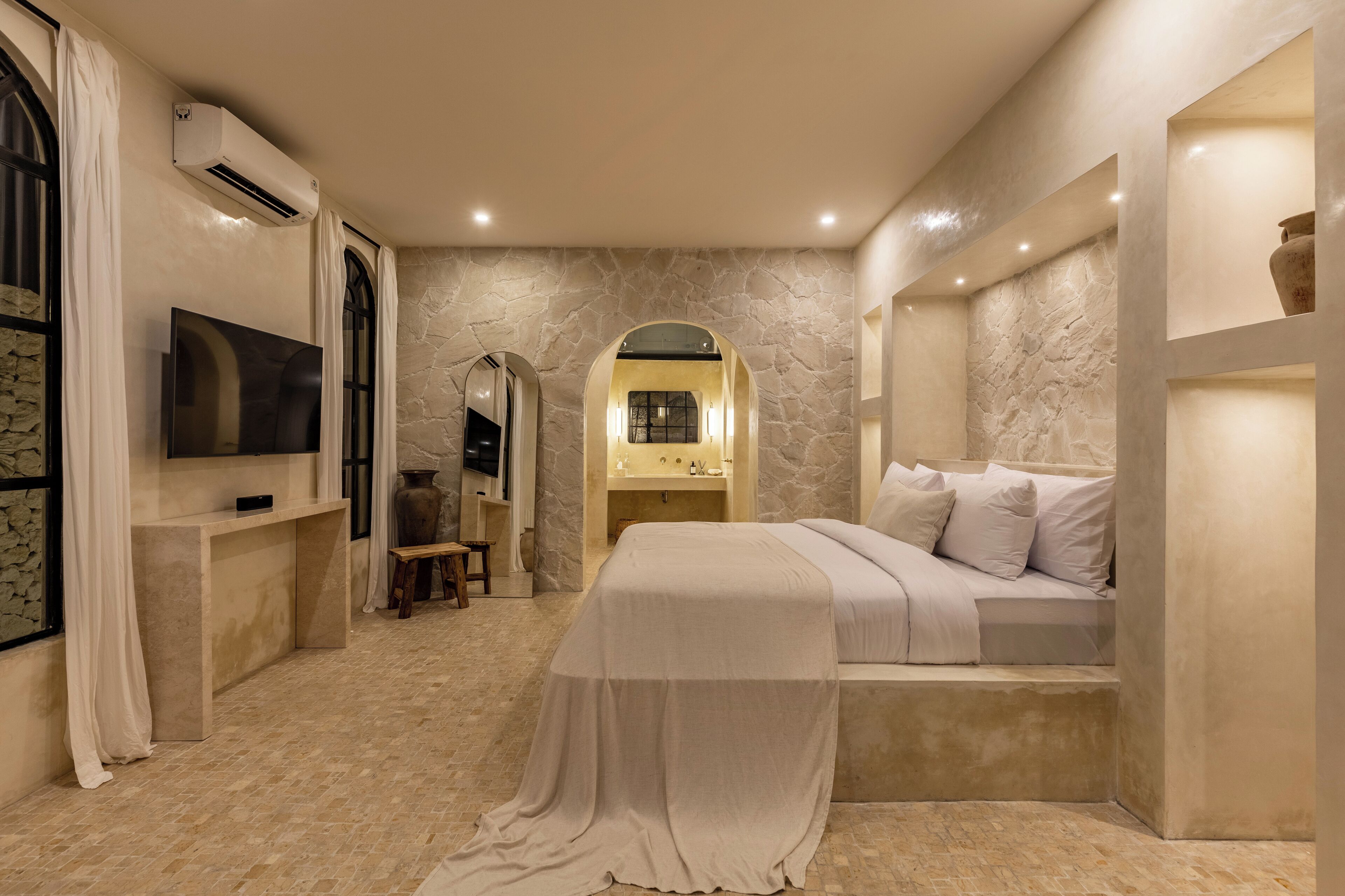 Quarto moderno com uma cama grande, televisão, penteadeira e parede de pedra.