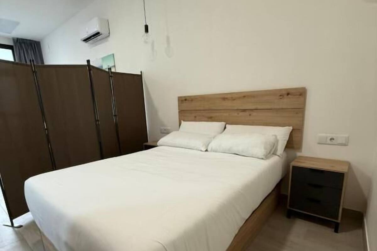 Quarto com cama de madeira, mesa de cabeceira, guarda-roupa e luminária no teto.