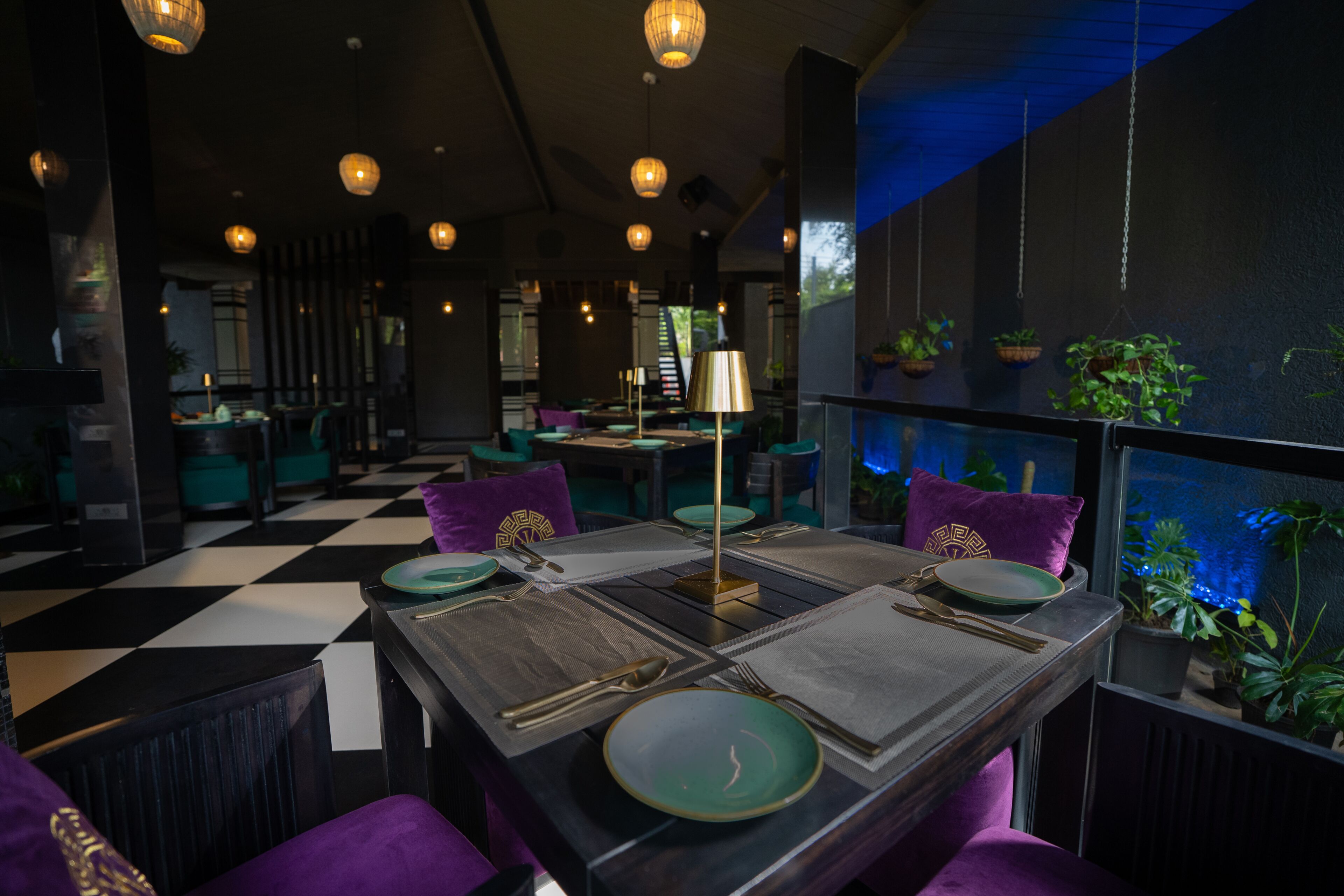 Interior de restaurante com chão quadriculado, mesas postas com pratos, talheres e um candeeiro.