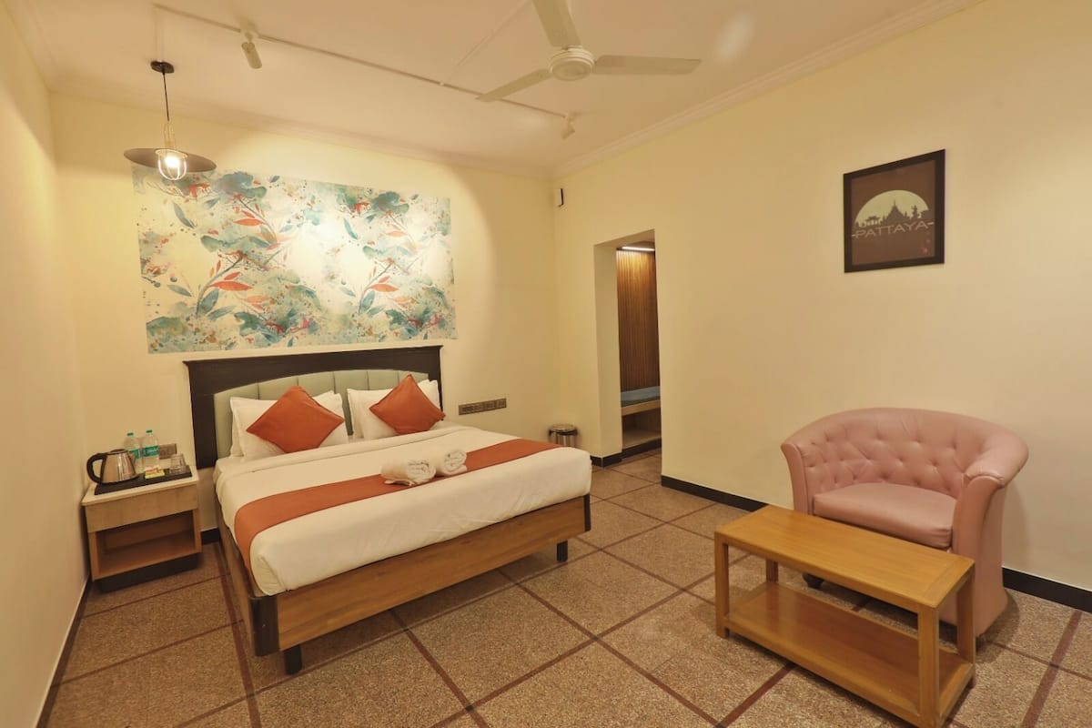 Quarto de hotel com cama, cadeira, mesa de cabeceira, obra de arte na parede e ventoinha no teto.