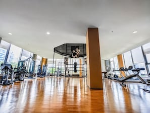 Uma academia com diversos equipamentos de exercício, janelas amplas e um pilar central.