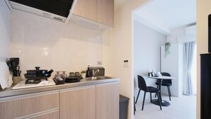 Cozinha moderna com fogão embutido, pia e armários. É visível uma área de refeições ao fundo, com mesa e cadeiras.