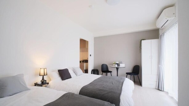 Quarto de hotel com duas camas, uma escrivaninha, cadeiras e aparelho de ar condicionado.