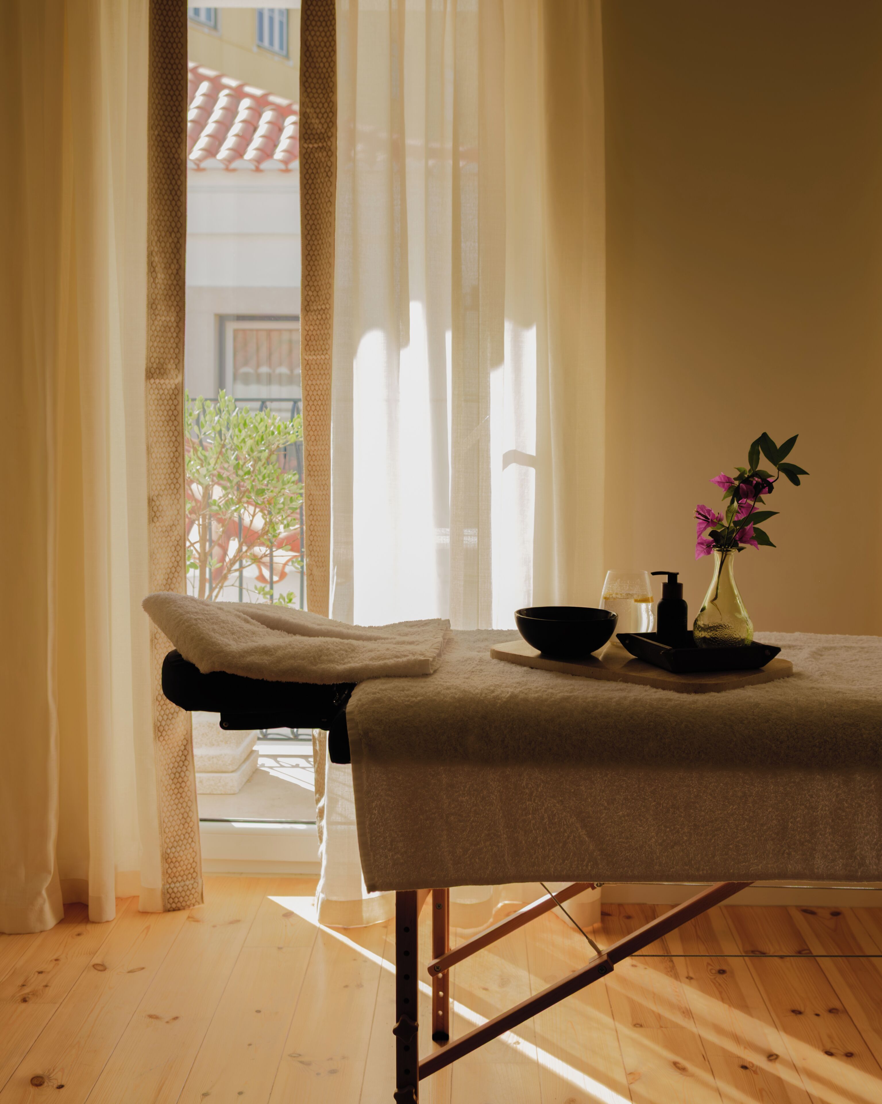 Quarto com mesa de massagem, um vaso de flores e vista para um edifício.