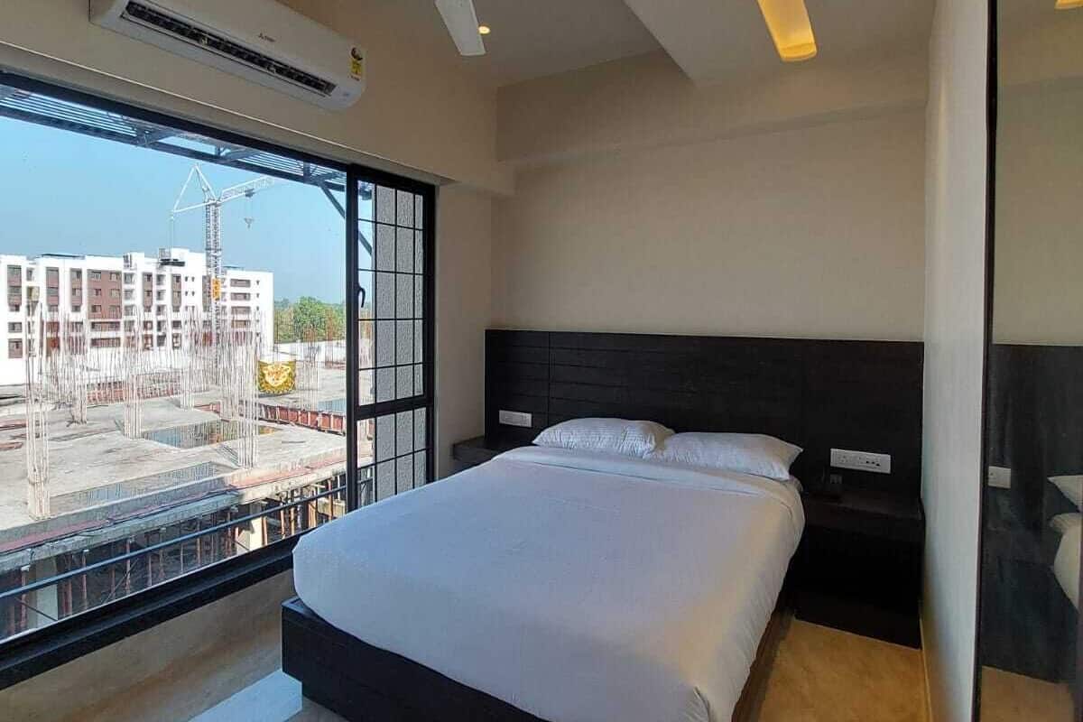 Quarto moderno com uma cama grande, um ventilador de teto e vista para uma obra por uma janela ampla.