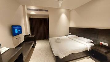 Quarto de hotel moderno com cama grande, mesas de cabeceira, TV e ventoinha no teto.