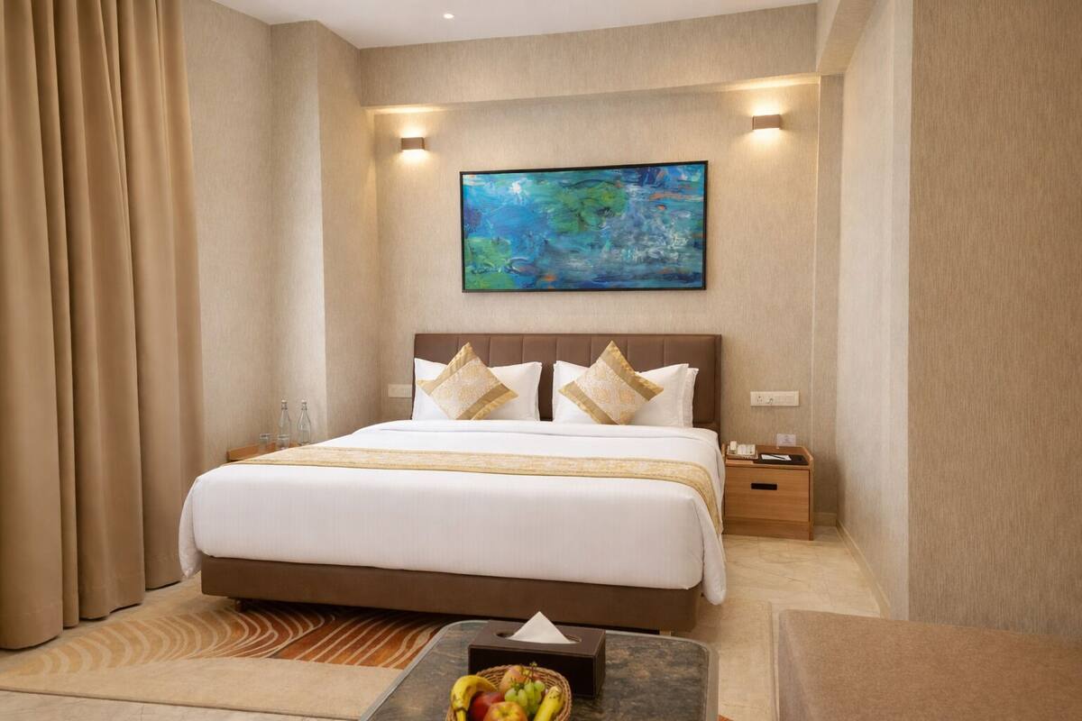 Quarto de hotel com uma cama grande, uma mesa de cabeceira, um quadro na parede e uma fruteira no chão.