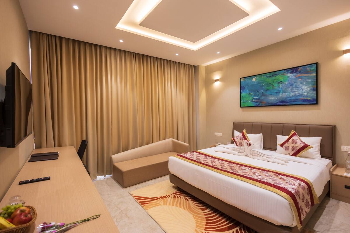 Quarto de hotel com uma cama, uma escrivaninha, uma televisão e um quadro na parede.