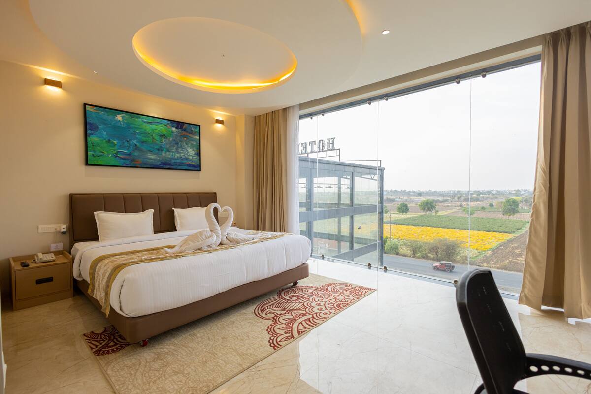 Quarto de hotel moderno com uma cama grande, um quadro, vista para o campo e varanda.