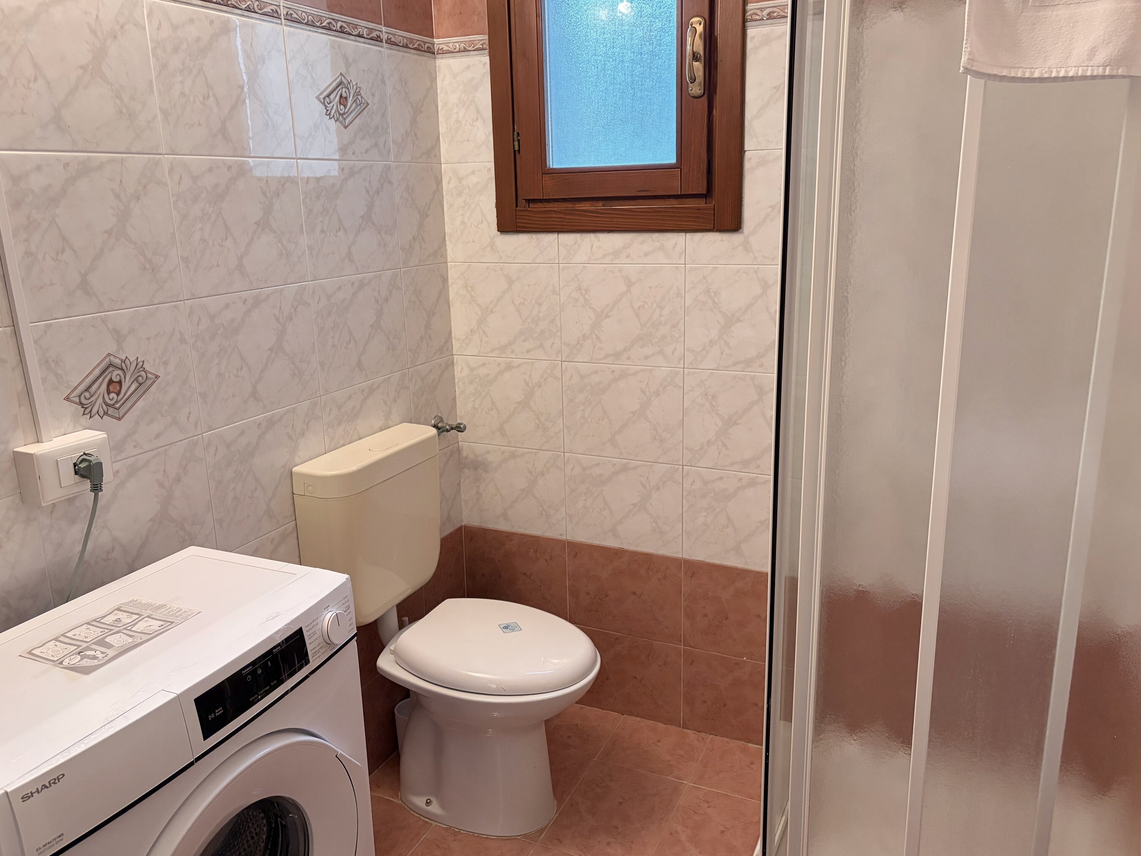 Casa de banho com máquina de lavar roupa, sanita e zona de duche.