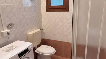 Casa de banho com máquina de lavar roupa, sanita e zona de duche.