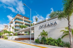 Um hotel moderno chamado OCEANA, com uma placa bem visível, uma estrutura de vários andares e uma área ajardinada com palmeiras.
