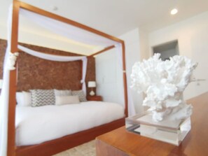 Quarto com cama de dossel, mesa de cabeceira e uma escultura branca decorativa sobre uma mesa de vidro.