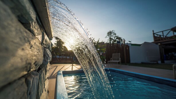 Piscina com água caindo sobre uma parede de pedra.