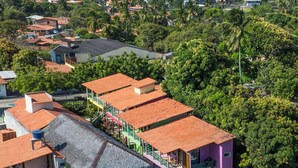 Um edifício grande, com vários andares, com piscina, rodeado por vegetação exuberante e outros edifícios residenciais.