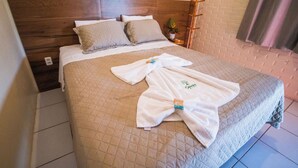 Cama bem arrumada com cobertura acolchoada, dois travesseiros e uma toalha dobrada em cima.