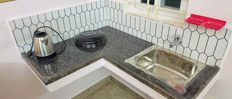 Cozinha compacta com bancada de granito, pia de aço inoxidável e janela com padrão de grade.