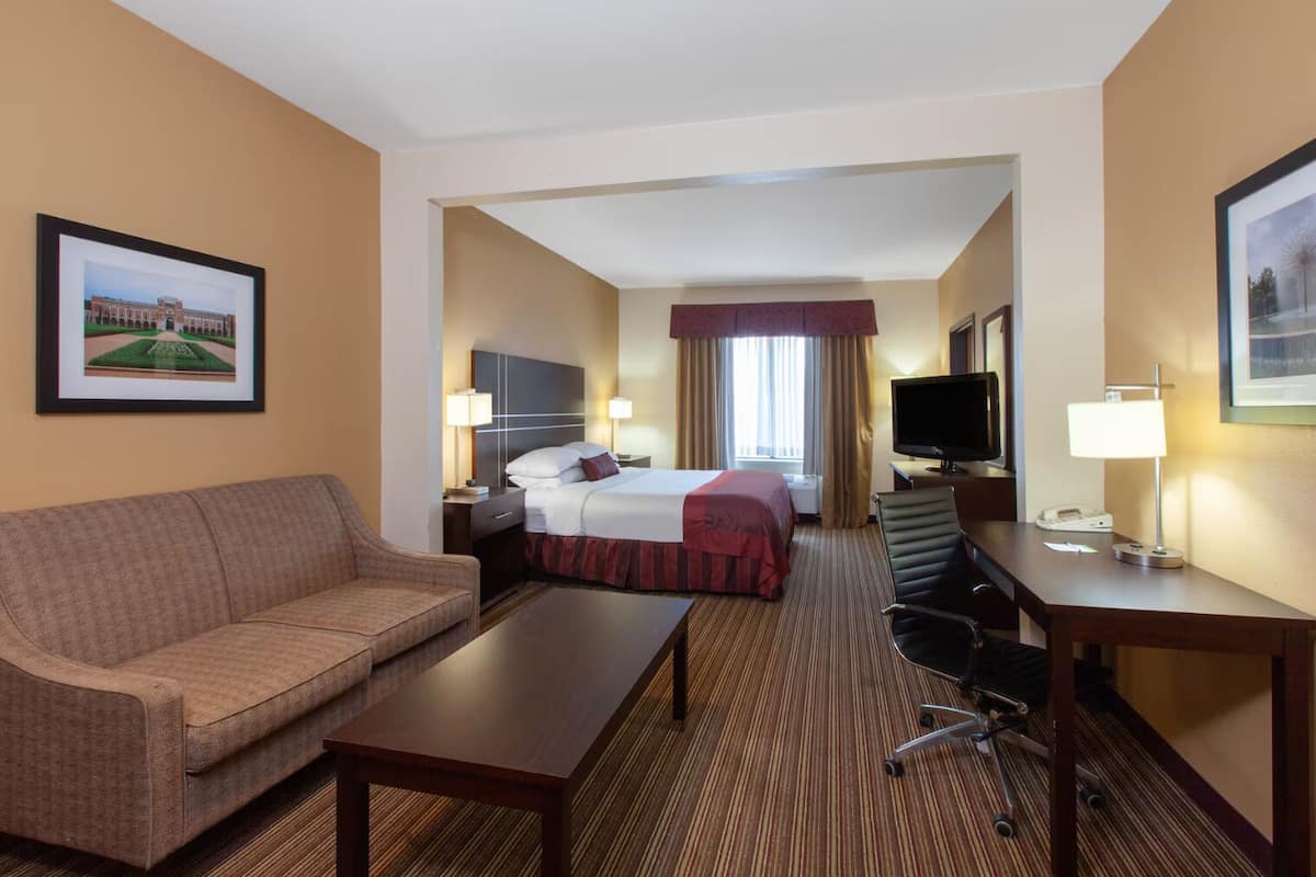 Quarto de hotel com cama, escrivaninha, cadeira, sofá e televisão.