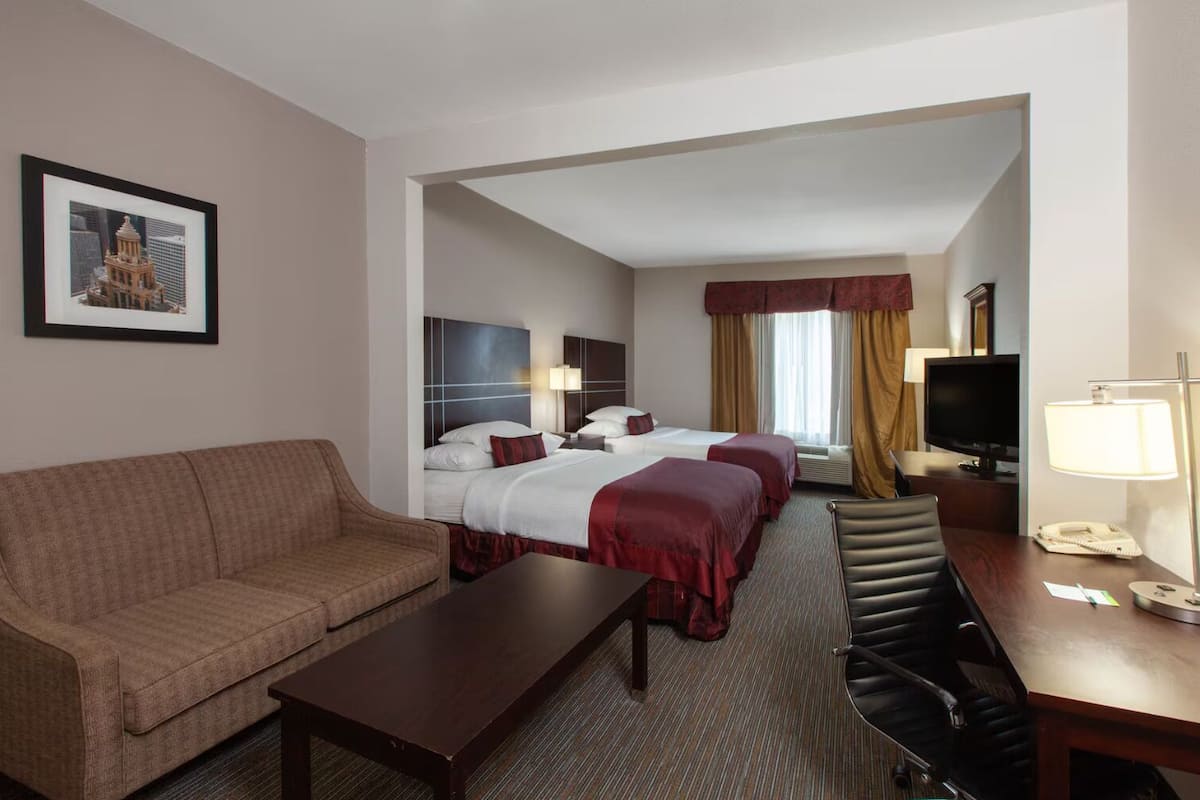 Quarto de hotel com sofá, duas camas individuais, escrivaninha, televisão e um quadro na parede.