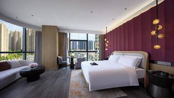 Quarto de hotel moderno com uma cama grande, um sofá, uma mesa de jantar e vista para edifícios altos.